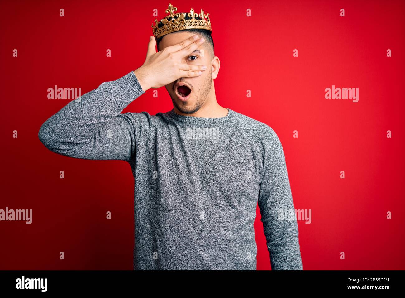 Young handsome man wearing golden crown of prince over isolated red ...