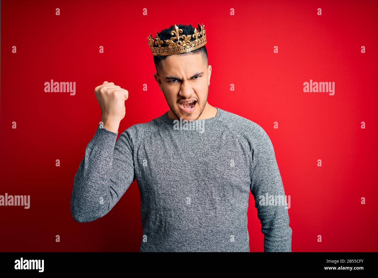 Young handsome man wearing golden crown of prince over isolated red ...