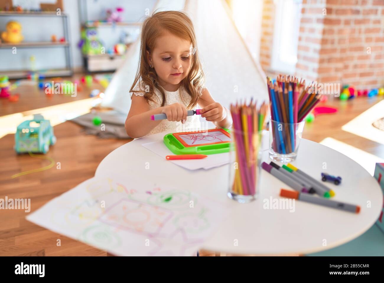 Adorable blonde toddler drawing using digital board around lots of toys ...