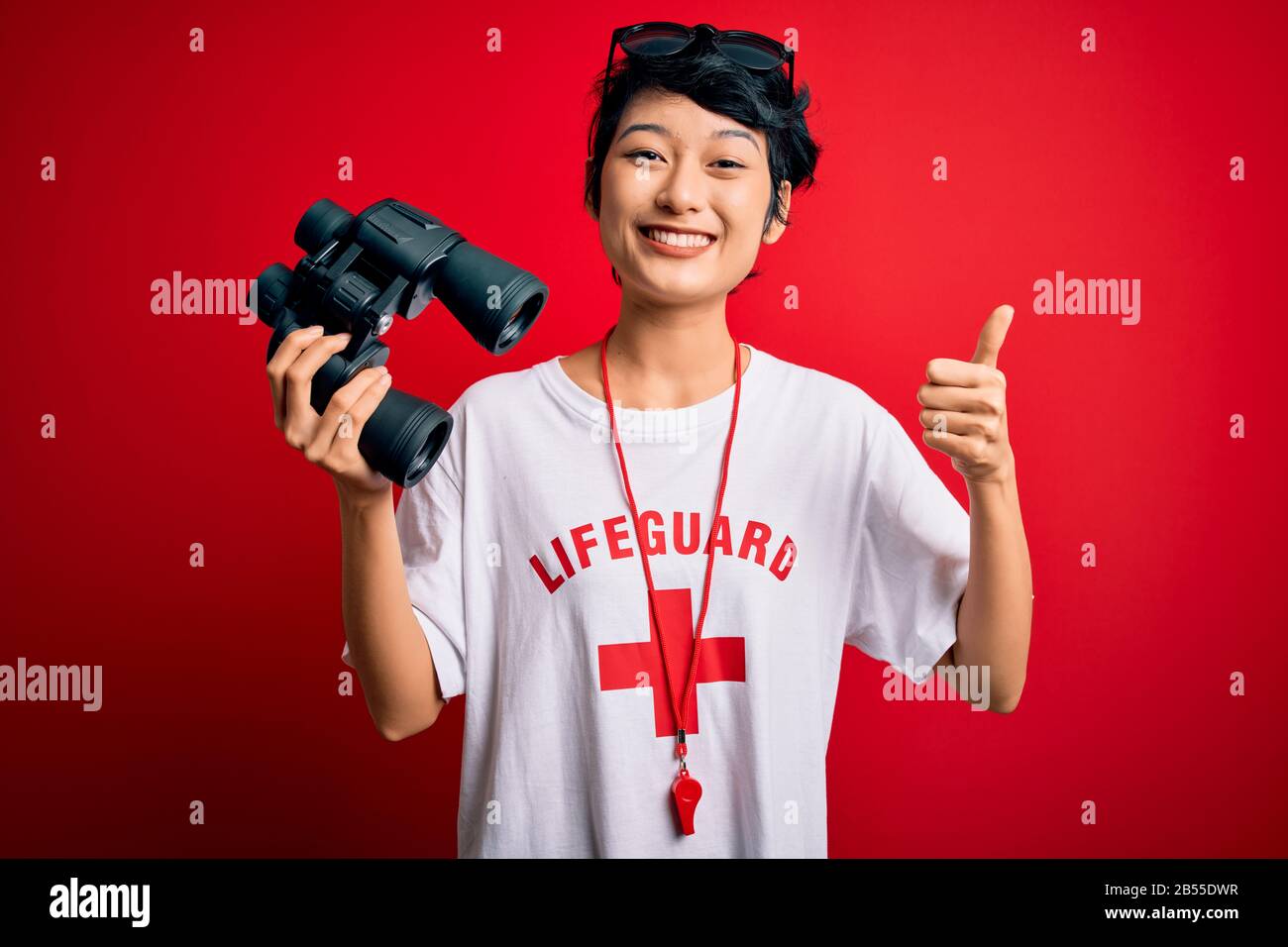 Young beautiful asian lifeguard girl using whistle and binoculars over ...