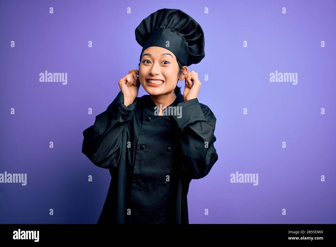 Young beautiful chinese chef woman wearing cooker uniform and hat over ...