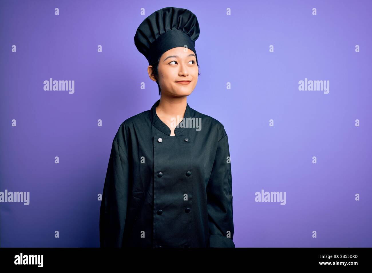 Young beautiful chinese chef woman wearing cooker uniform and hat over ...