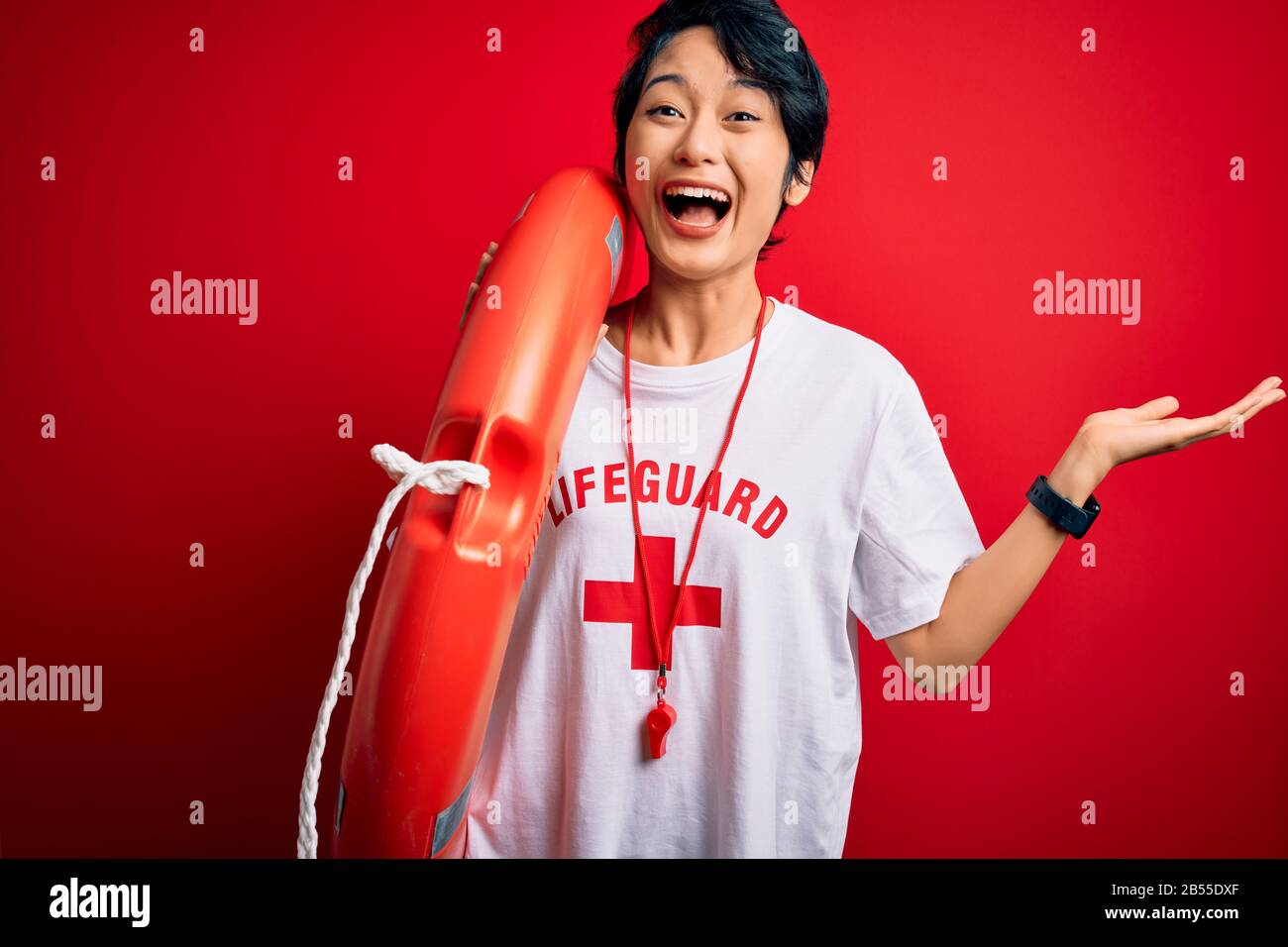 Young beautiful asian lifeguard girl using whistle holding orange float ...