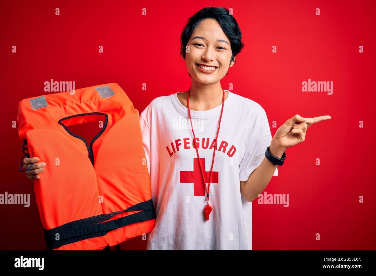 Young beautiful asian lifeguard girl using whistle holding orange life ...