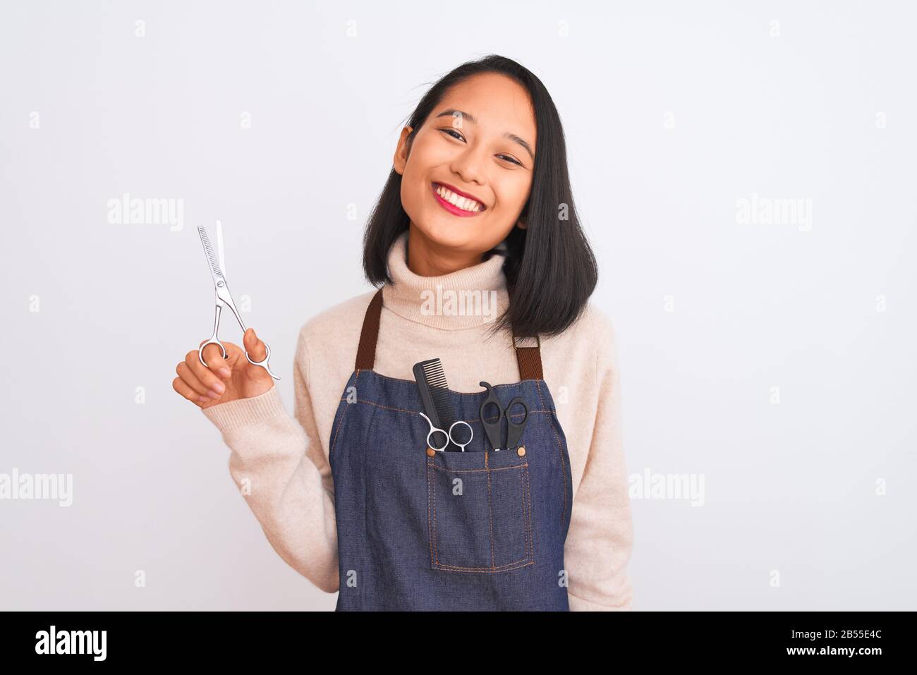 Chinese hairdresser woman wearing apron holding scissors over isolated white background with a ...