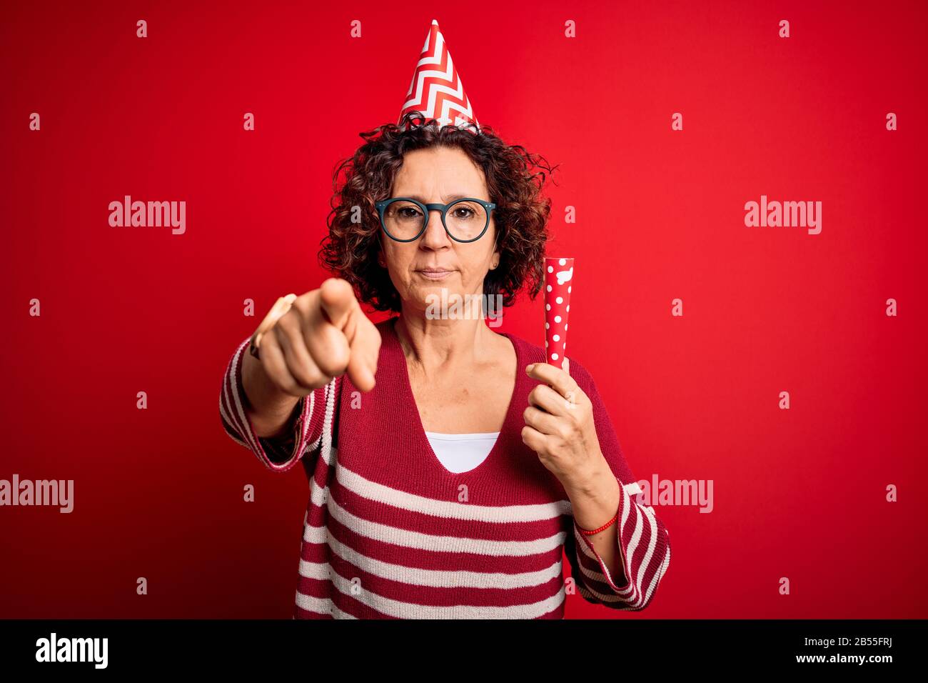 Middle age curly hair woman wearing birthday funny hat holding party ...