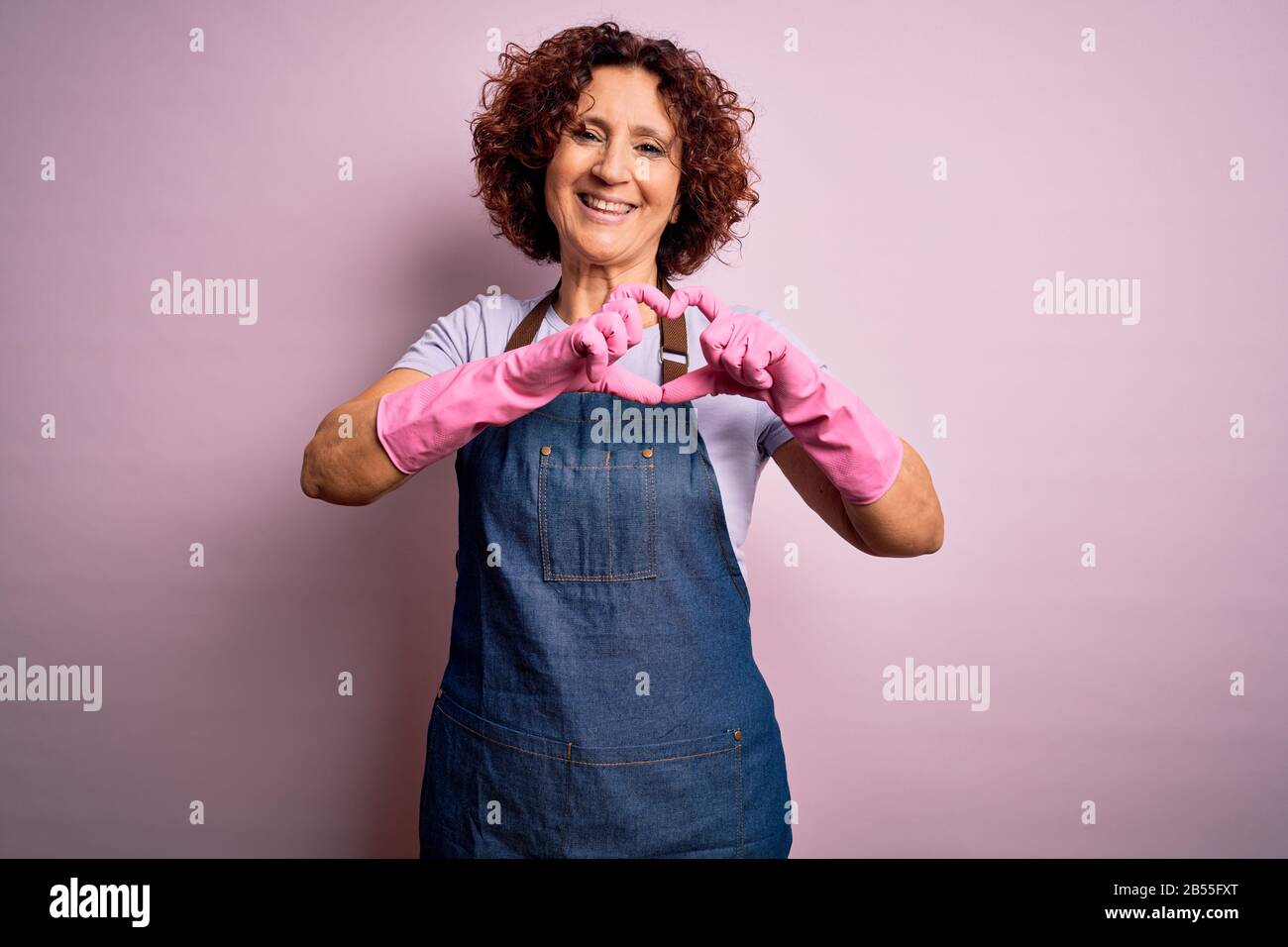 Middle age curly hair woman cleaning doing housework wearing apron and ...