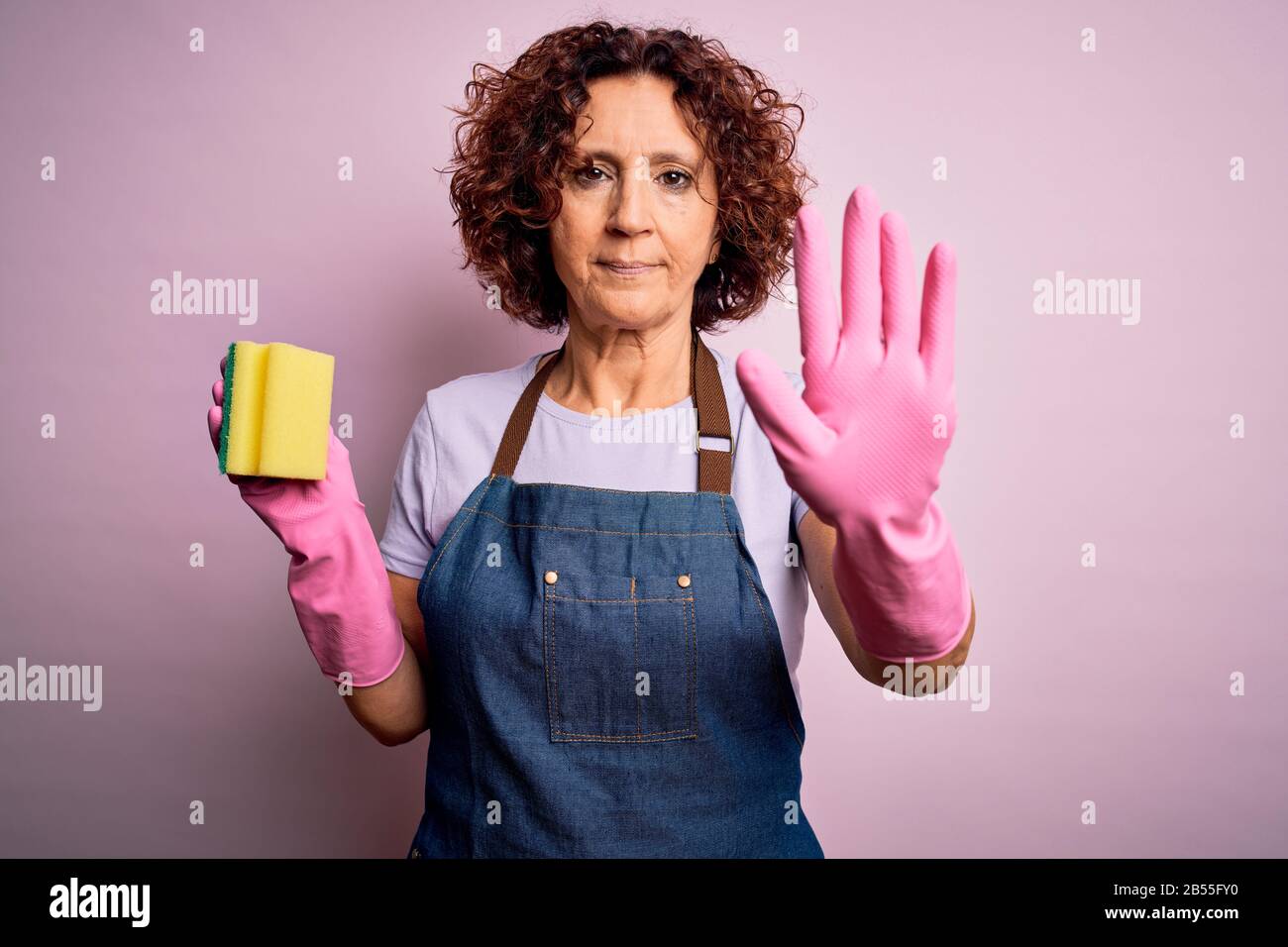 Middle age curly hair woman cleaning doing housework wearing apron and ...