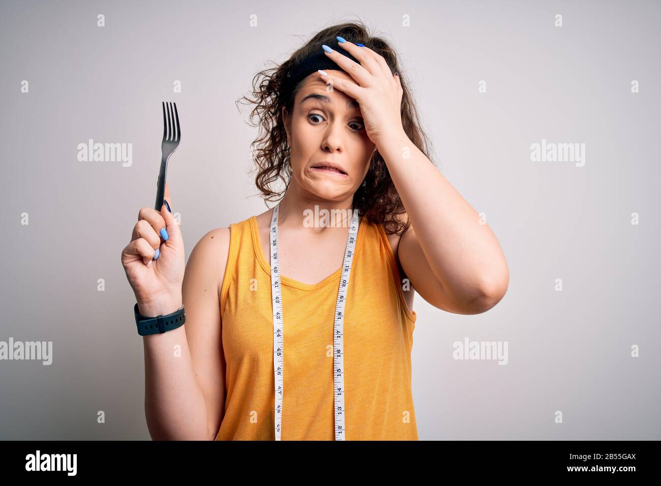 Young beautiful woman with curly hair doing diet holding fork and tape ...