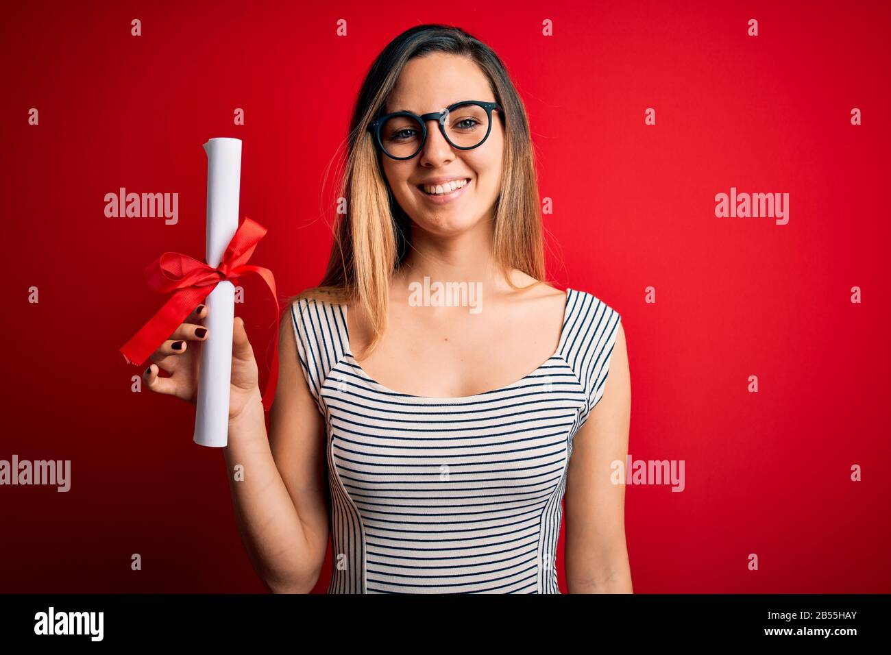 Young blonde woman with blue eyes wearing glasses holding graduated ...