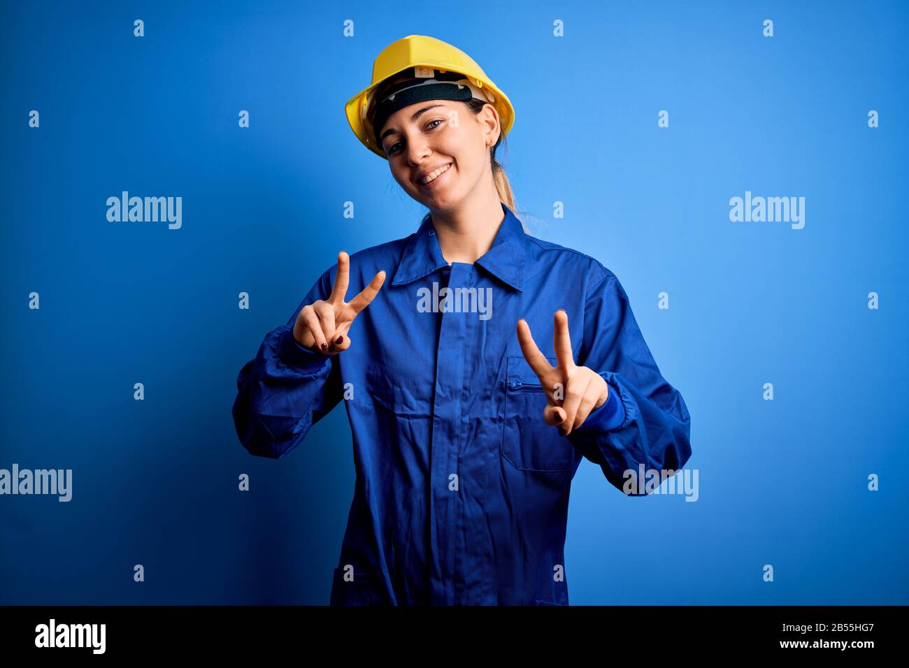 Young beautiful worker woman with blue eyes wearing security helmet and ...