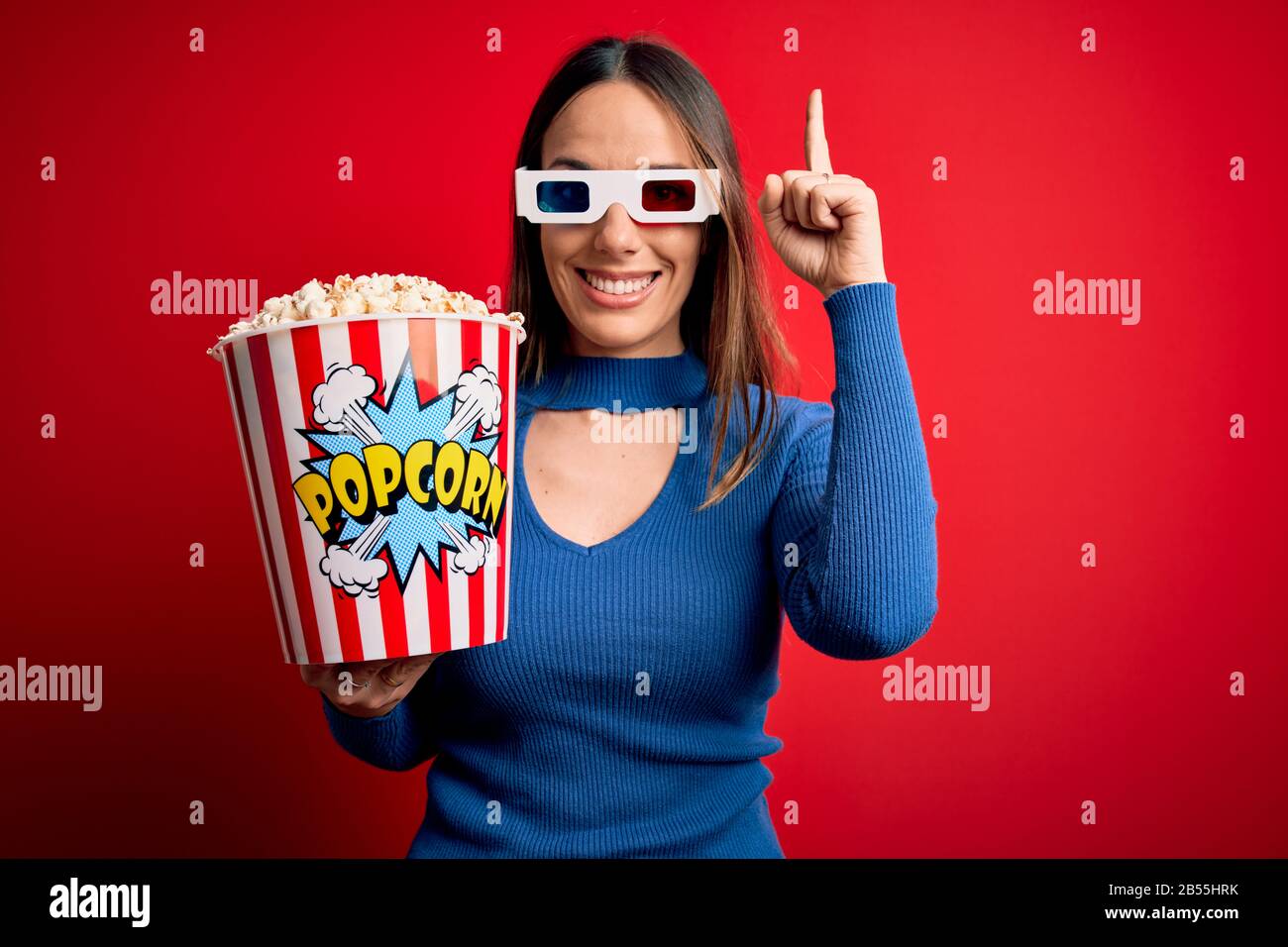 Young blonde woman wearing 3d glasses and eating pack of popcorn watching a movie on cinema ...