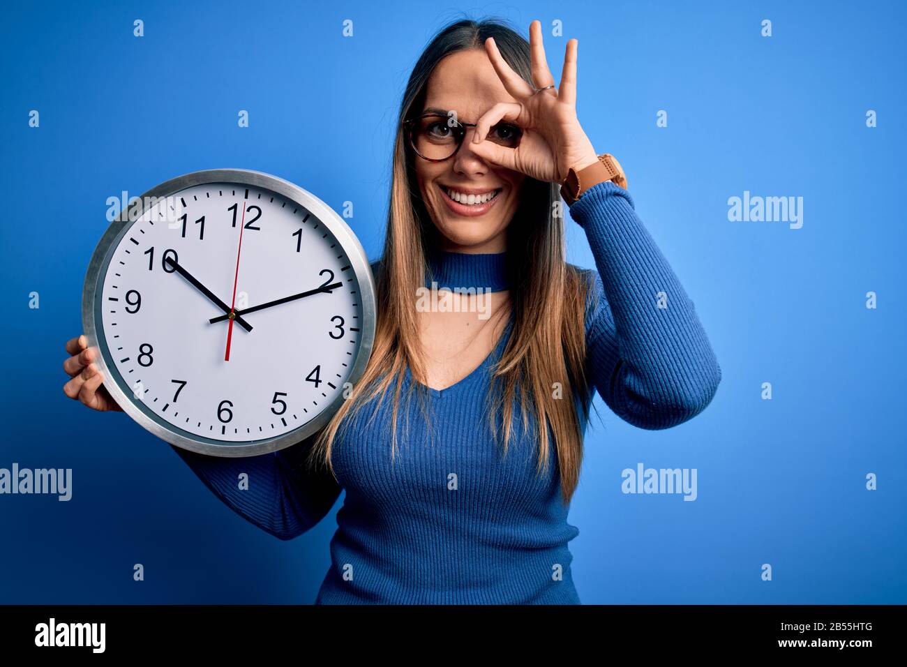 Young blonde woman with blue eyes holding big minute clock over ...