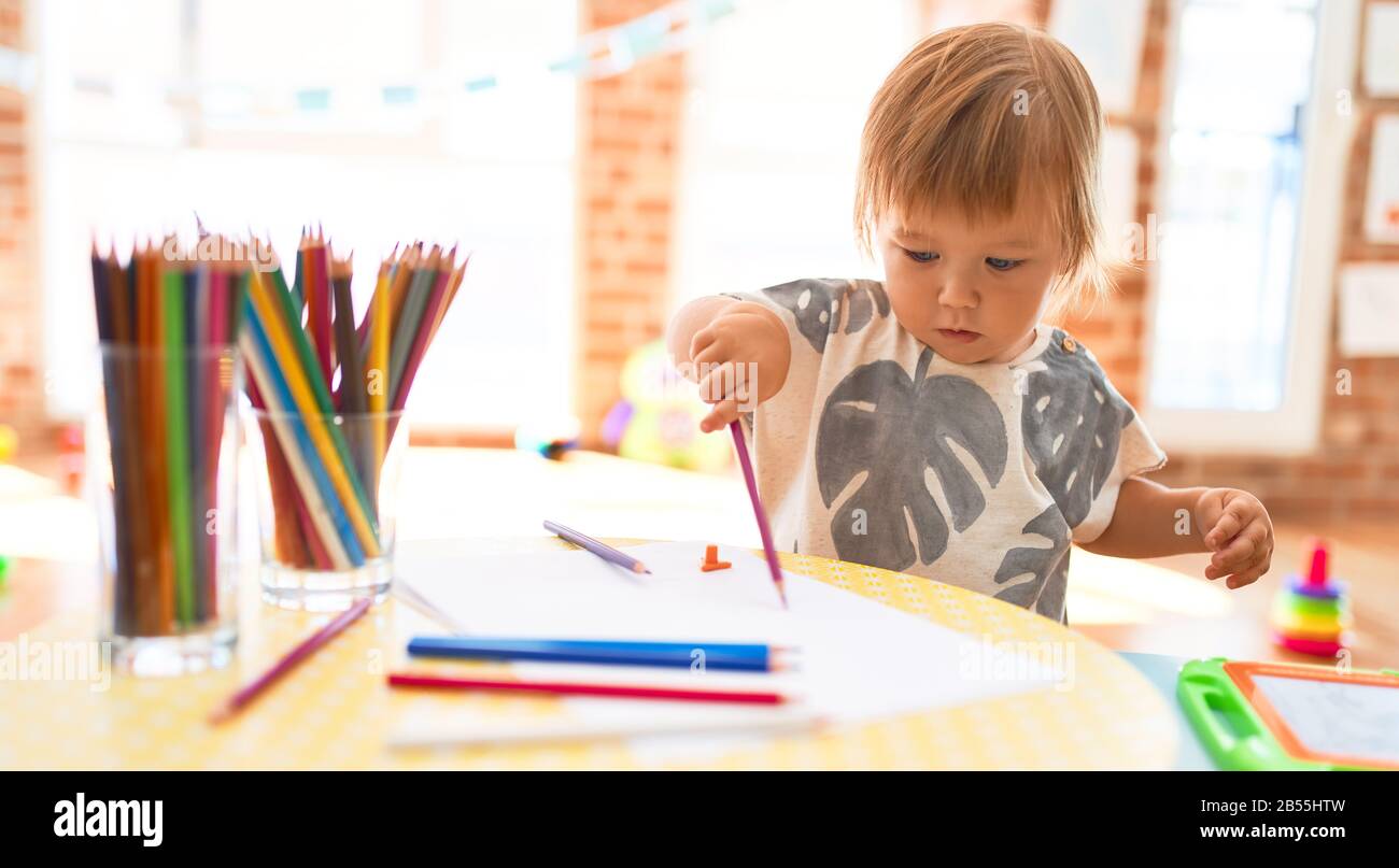 Adorable toddler drawing using paper and pencil around lots of toys at ...