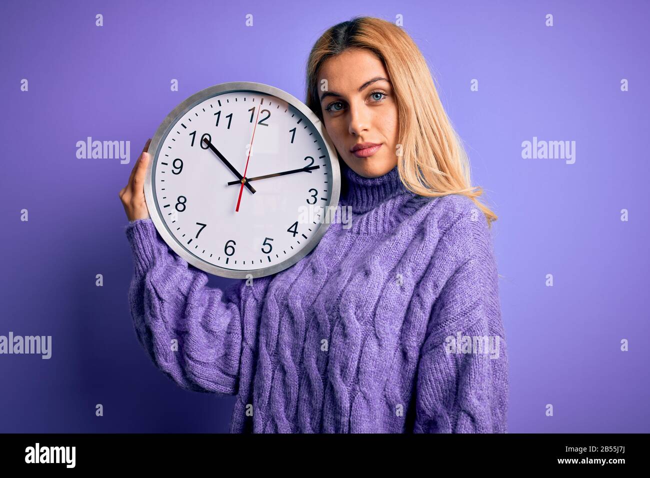 Young beautiful blonde woman doing countdown holding big clock over ...