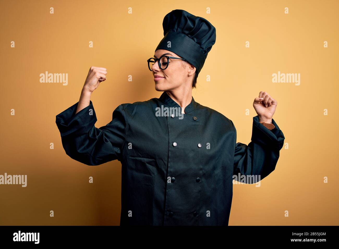 Young beautiful brunette chef woman wearing cooker uniform and hat over ...
