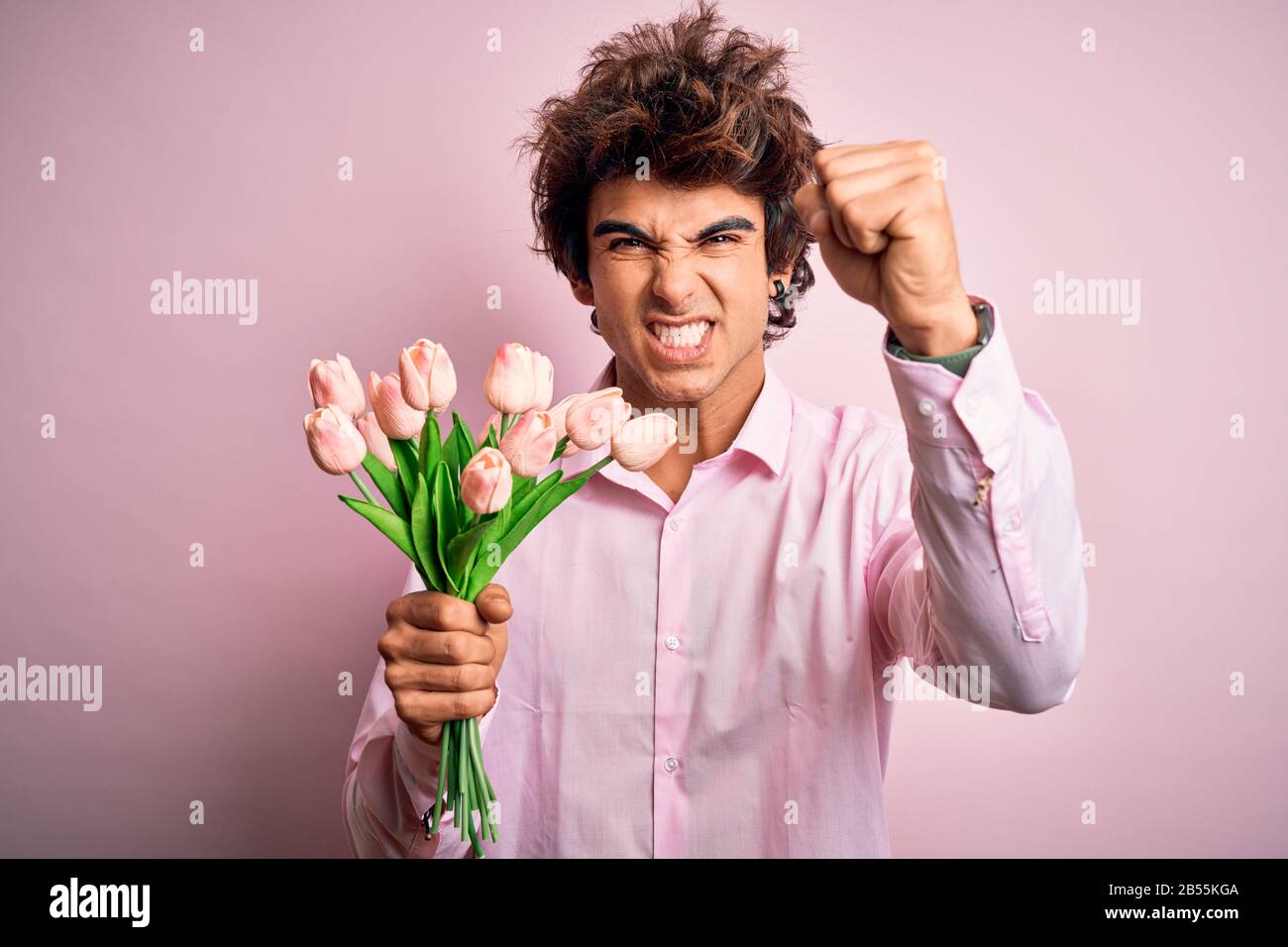 Young handsome man holding flowers standing over isolated pink ...