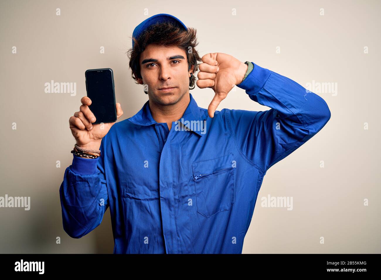 Young mechanic man wearing uniform holding smartphone over isolated ...