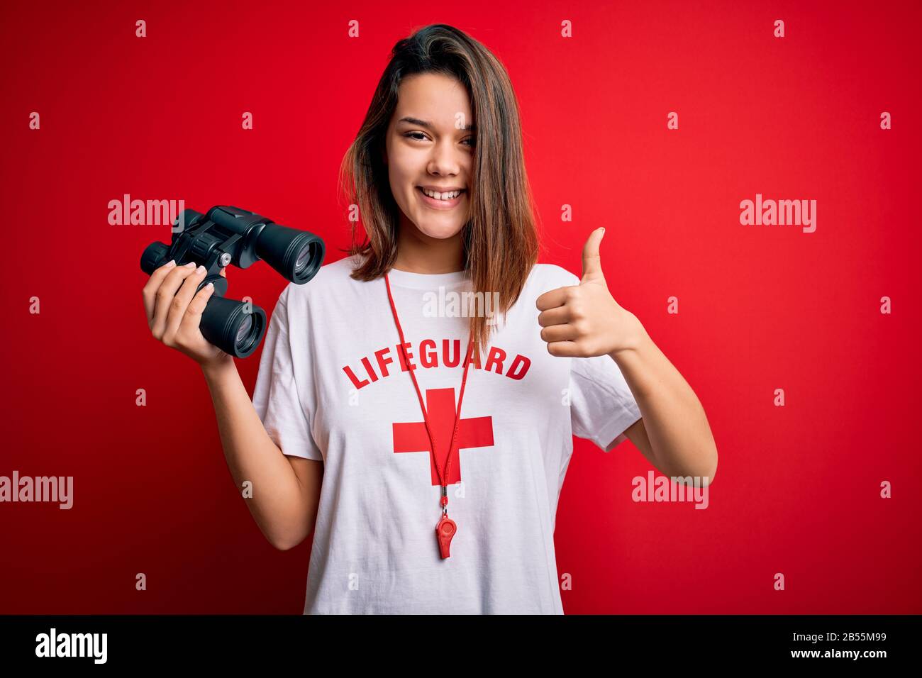 Young beautiful lifeguard girl wearing whistle using binoculars over ...