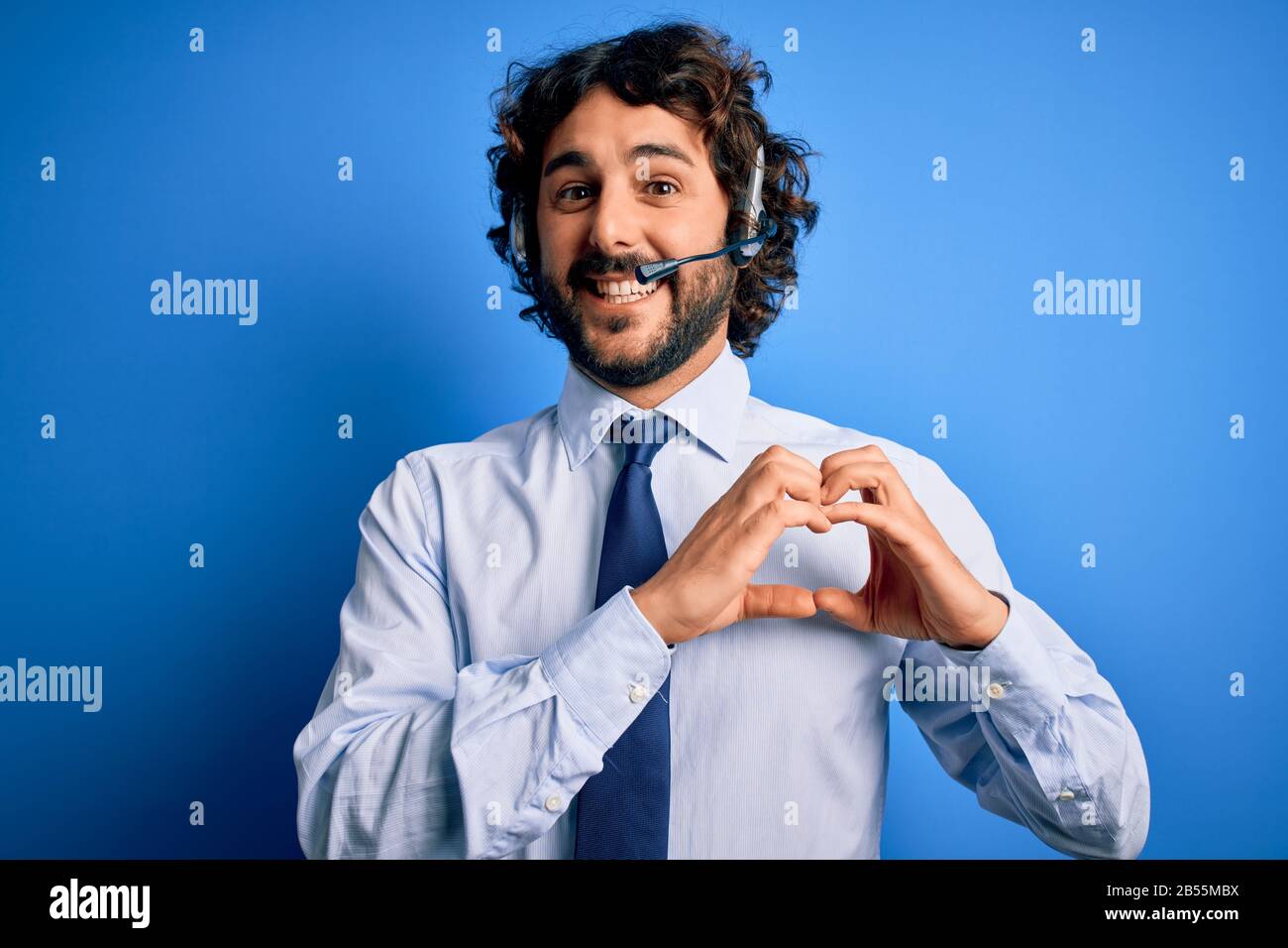 Young handsome call center agent man with beard working using headset over blue background ...