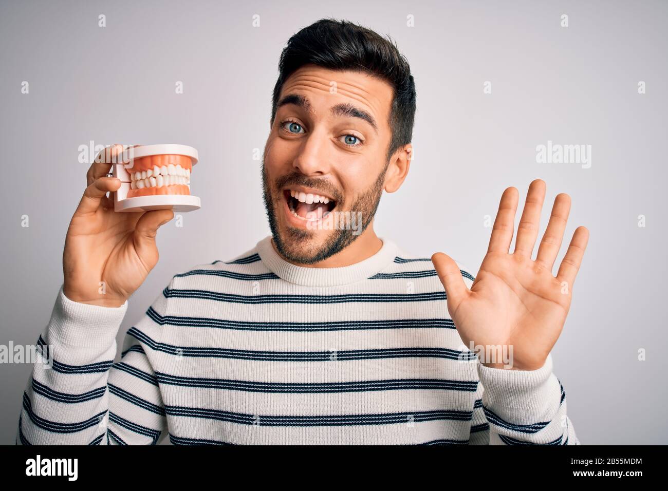 Young handsome man with beard holding plastic denture teeth over white ...