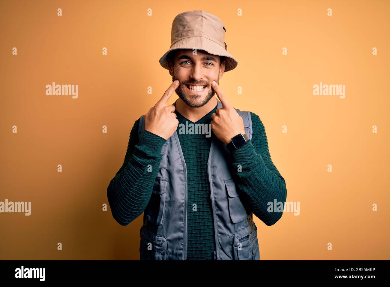 Handsome tourist man with beard on vacation wearing explorer hat over ...