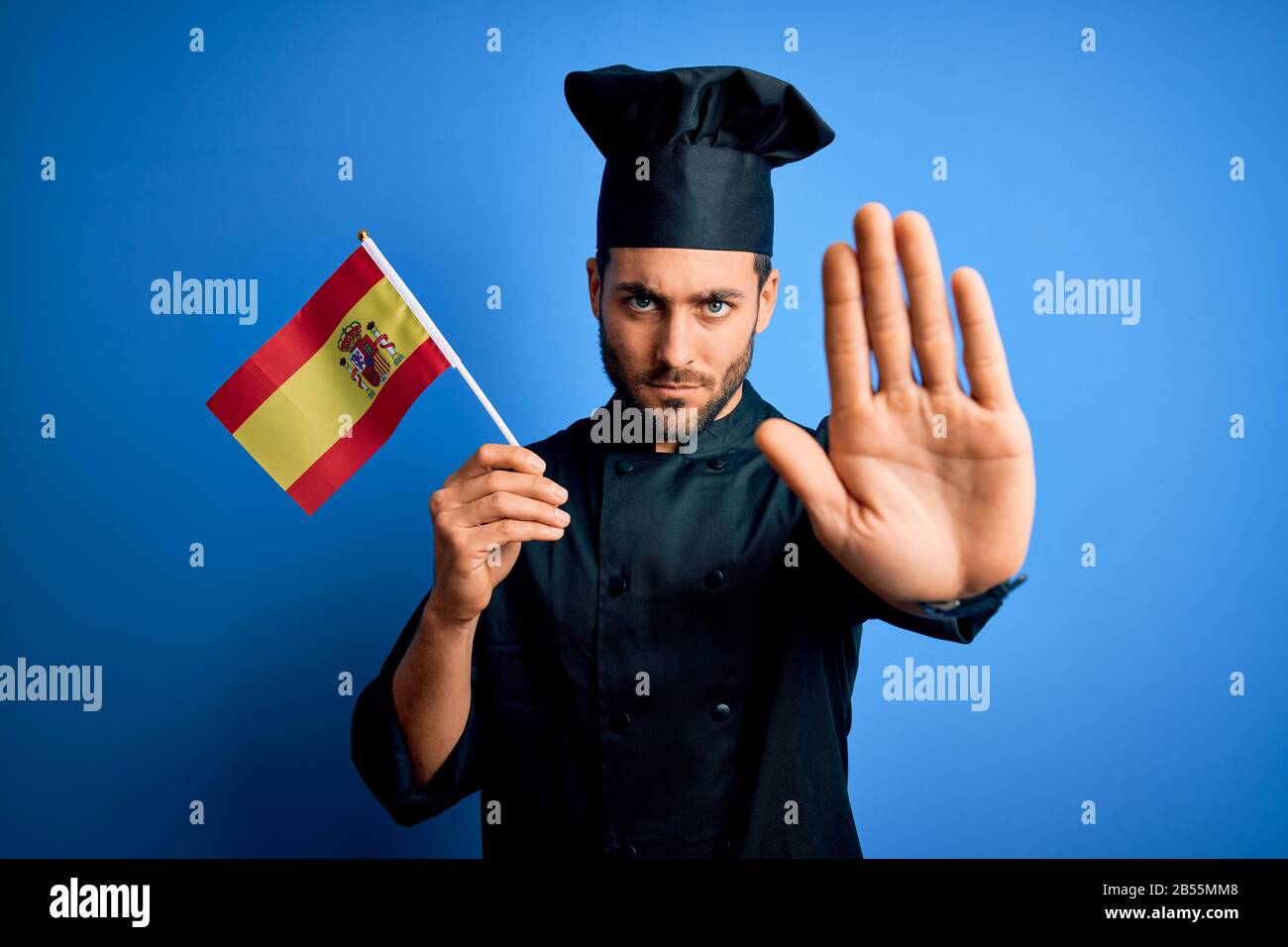 Young handsome cooker man with beard wearing uniform holding spain ...