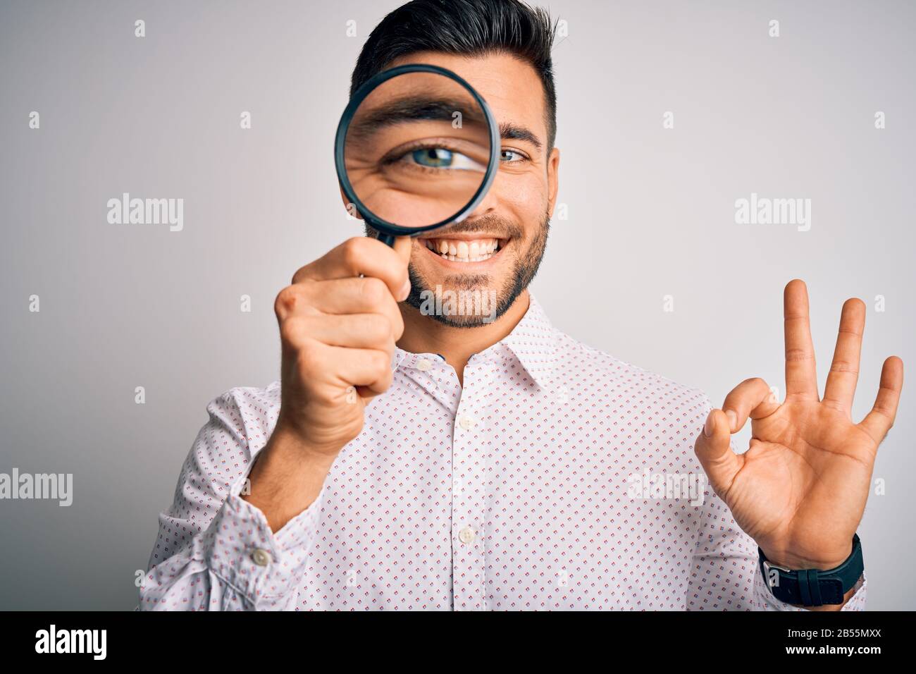 Young detective man looking through magnifying glass over isolated ...