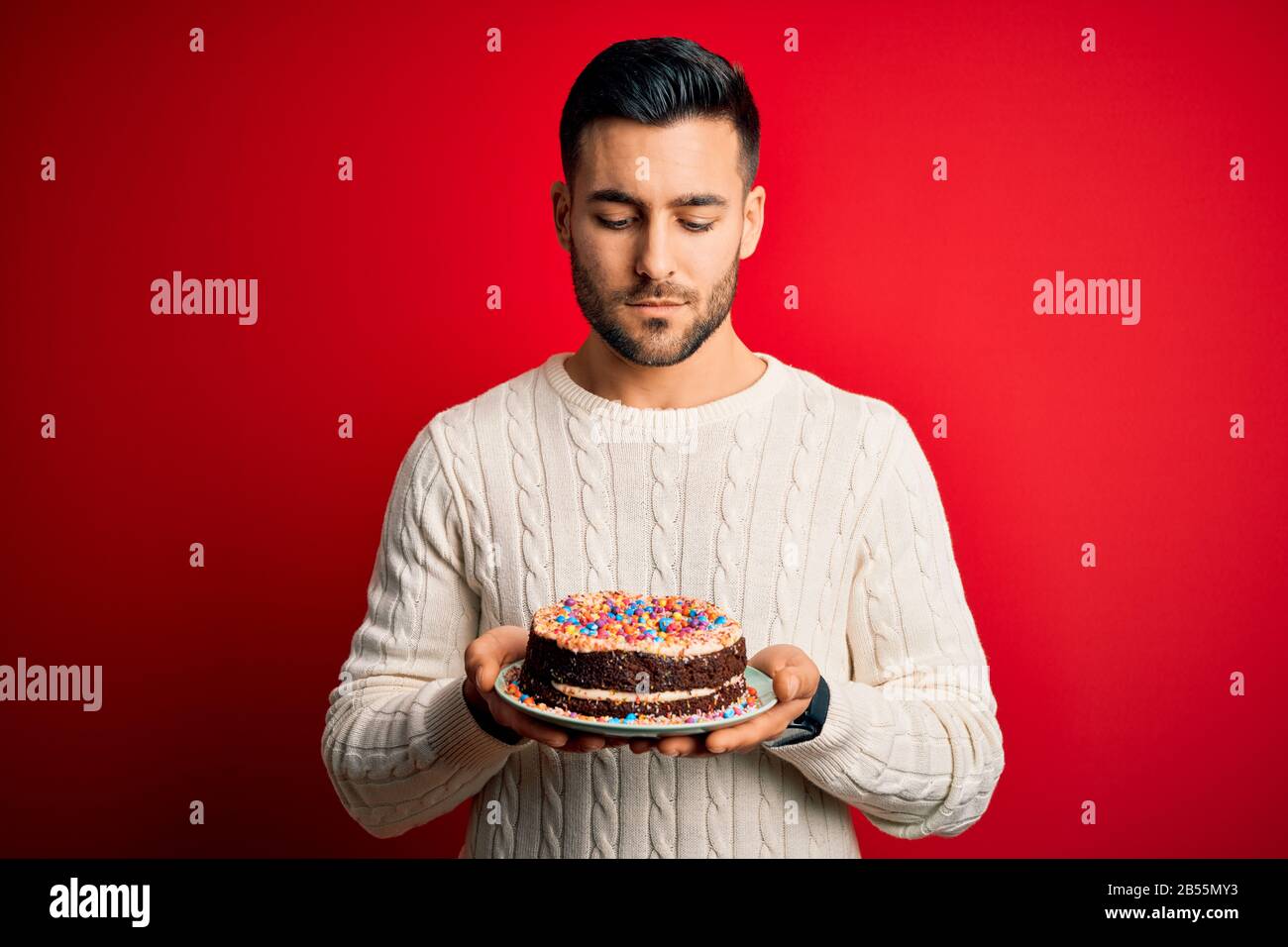 Young handsome man holding colorful birthday sweet cake over red ...