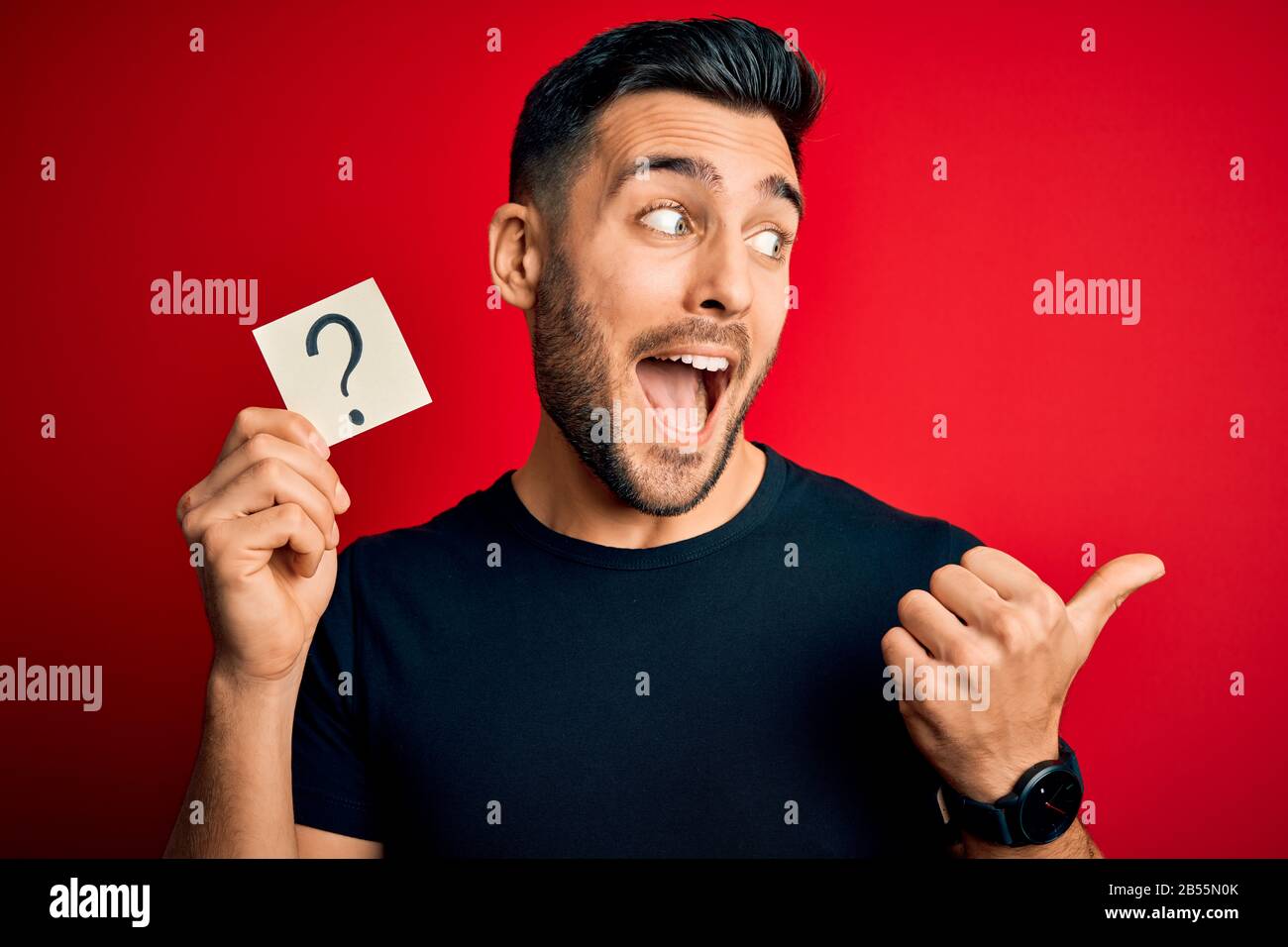 Young handsome man holding paper with question mark symbol over red ...