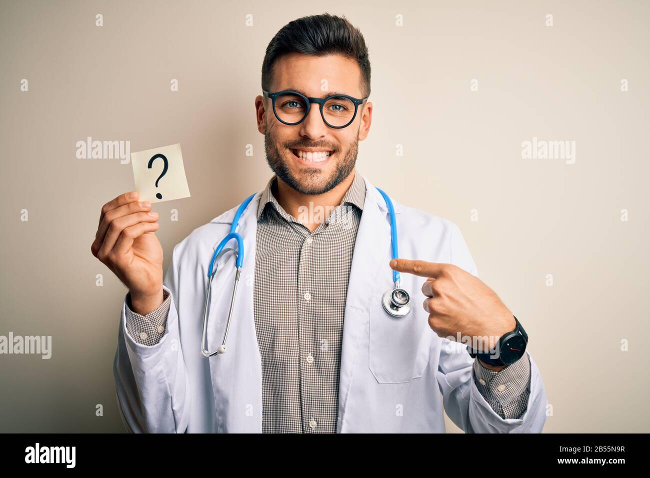 Young doctor man wearing stethoscope holding question mark reminder ...
