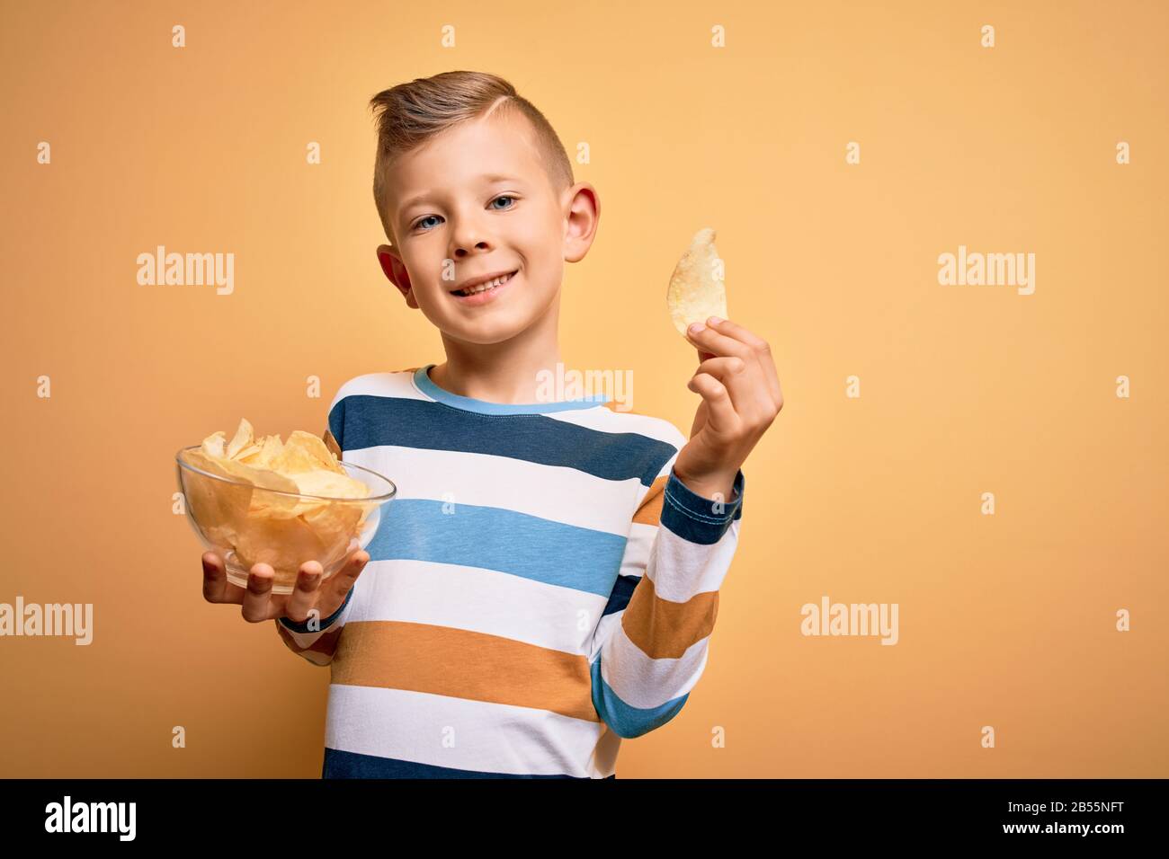 Young little caucasian kid eating unheatlhy potatoes crisps chips over ...