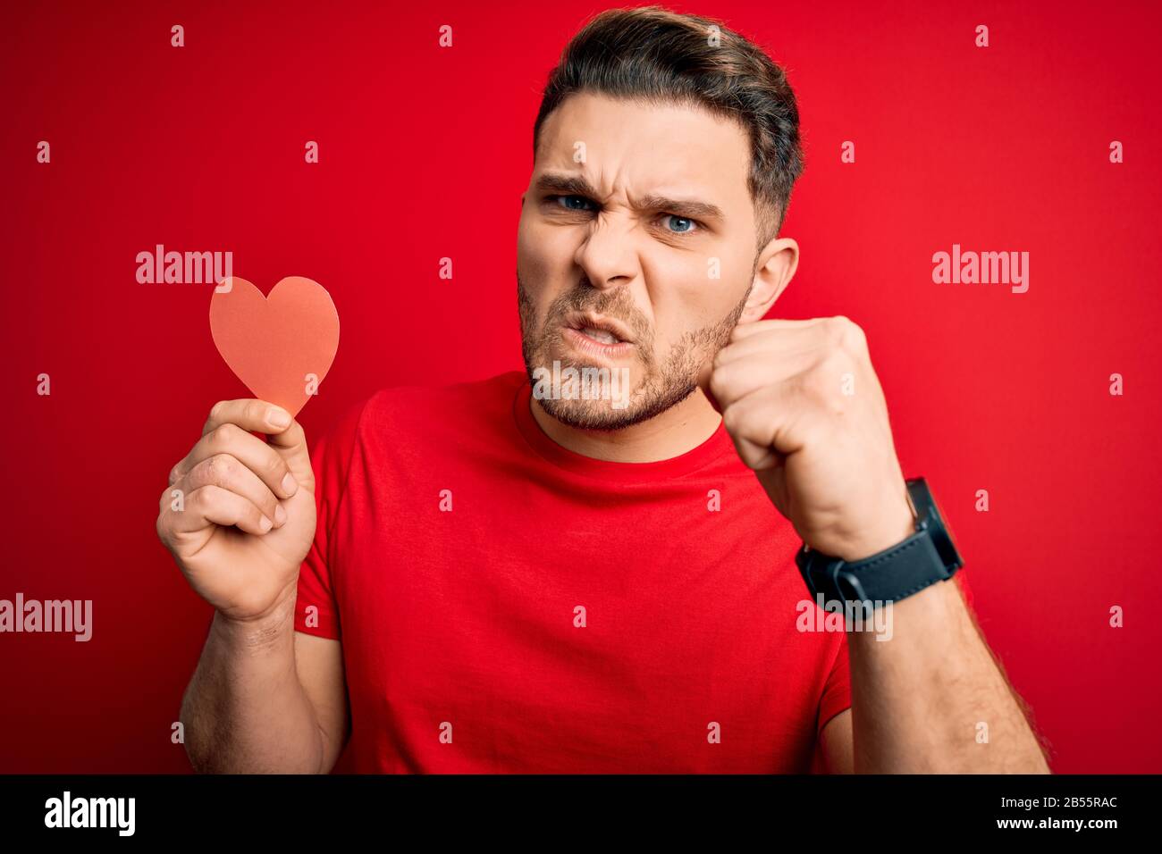 Young romantic man with blue eyes holding red heart paper shaped over ...