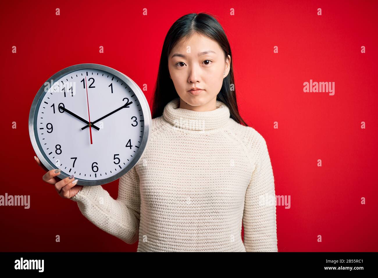 Young asian woman holding countdown big clock over red isolated ...