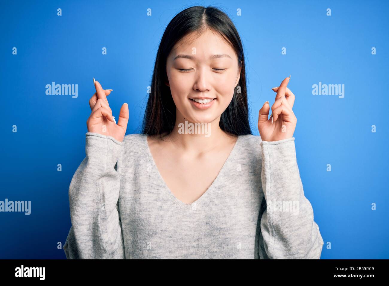 Young beautiful asian woman wearing casual sweater standing over blue ...