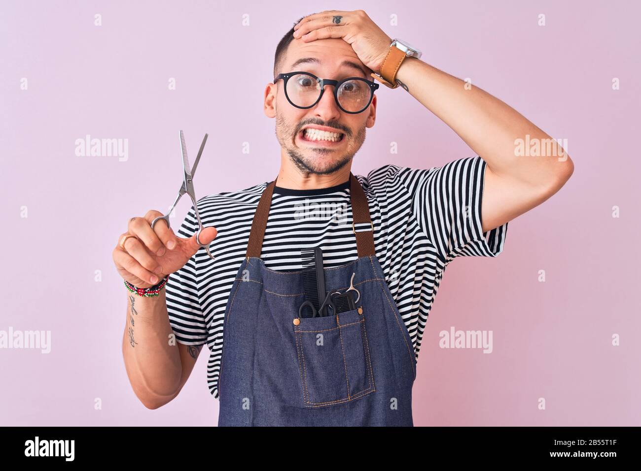 Young handsome hairdresser man wearing apron over pink isolated ...