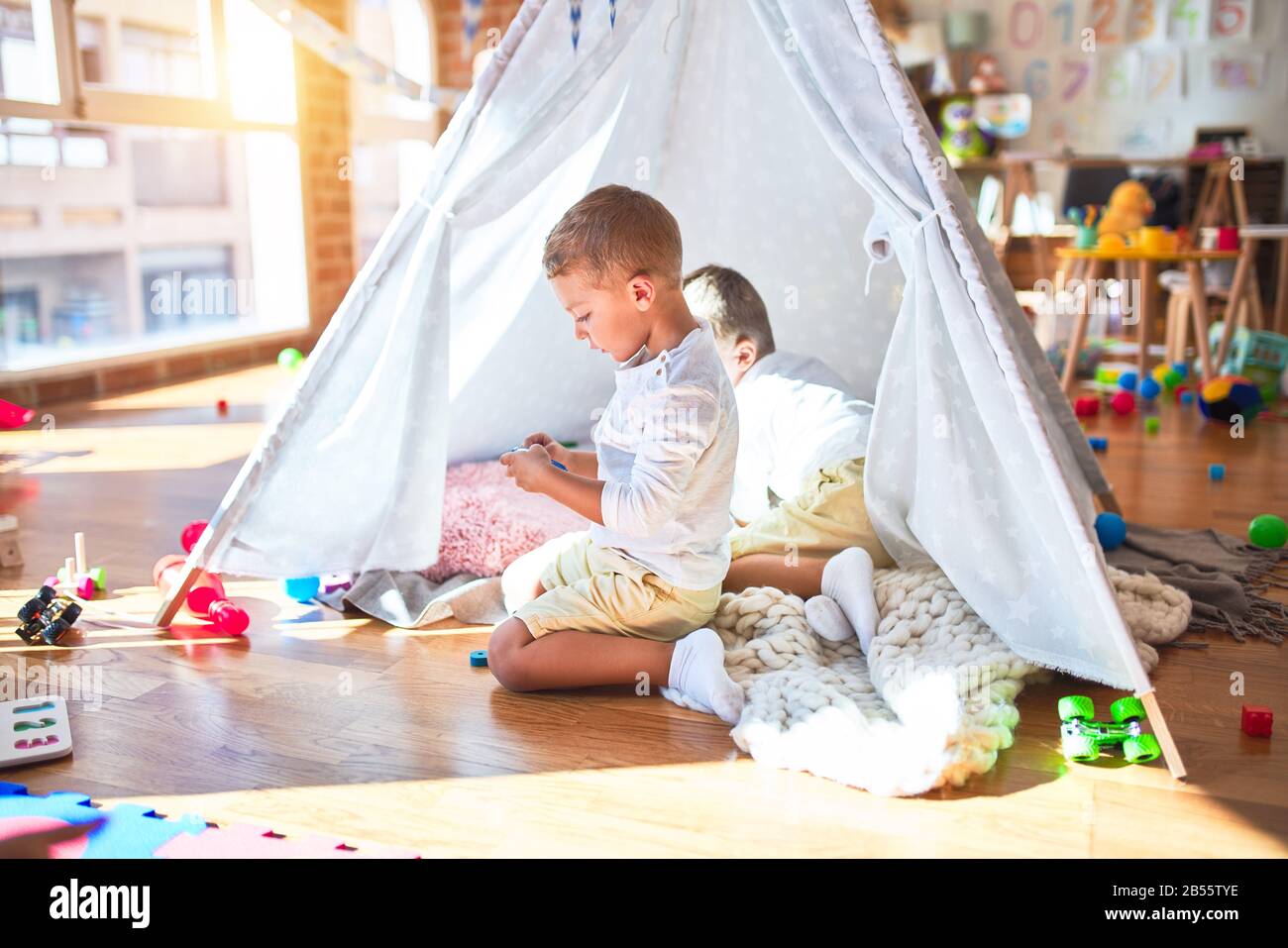 Adorable blonde twins playing inside tipi around lots of toys at ...