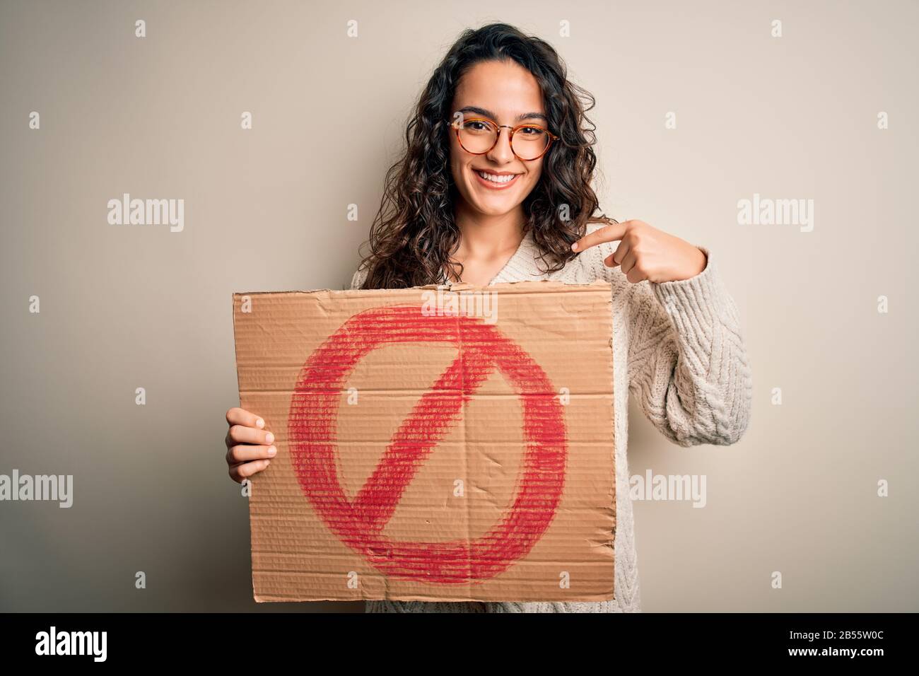Young beautiful woman with curly hair holding banner with prohibited ...