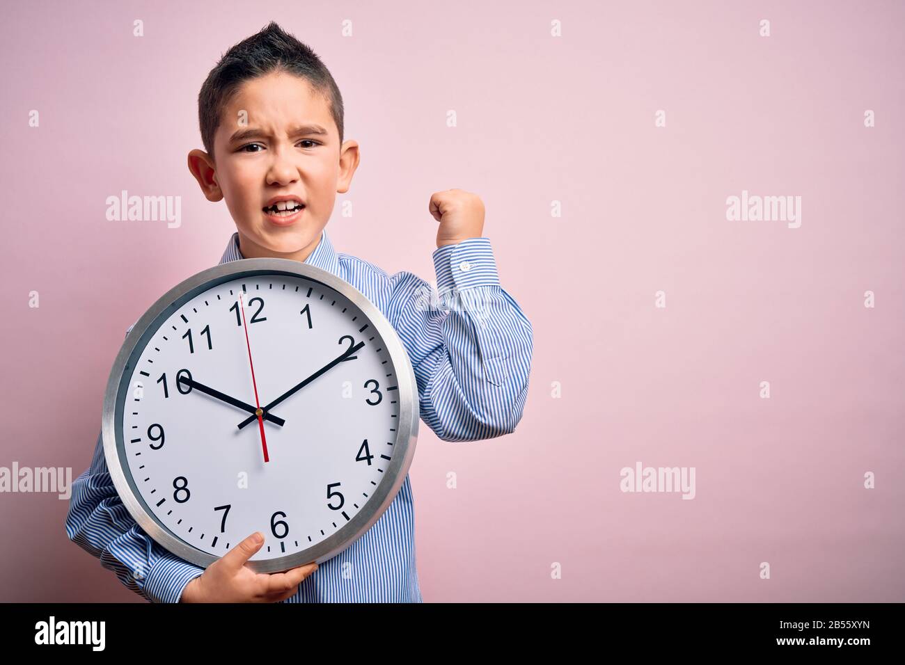 Young little boy kid holding big minute clock over isolated pink ...