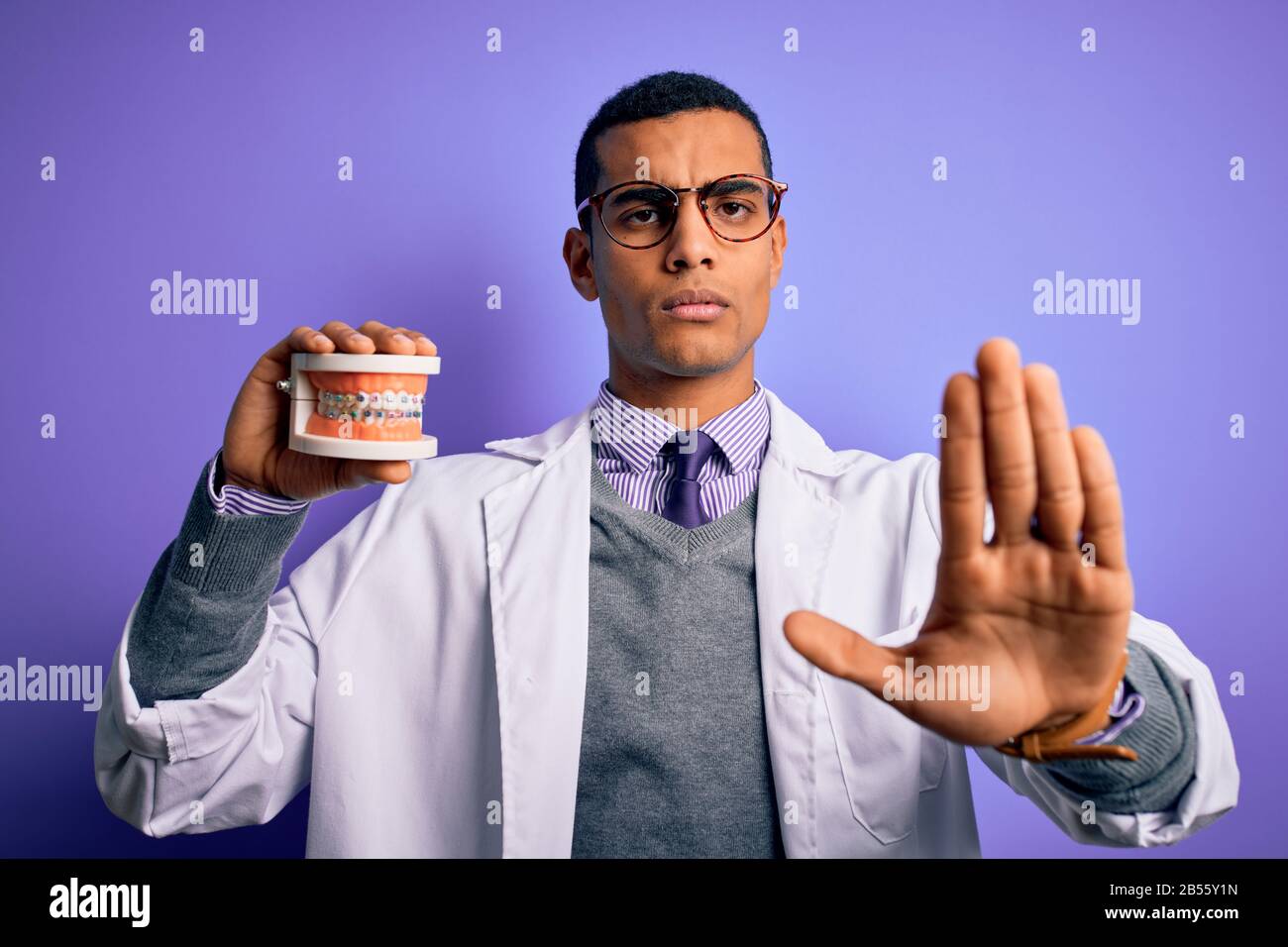 Young handsome african american dentist man holding denture teeth with ...