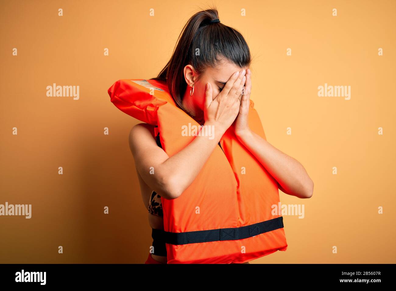 Young beautiful brunette woman wearing orange safe lifejacket over ...