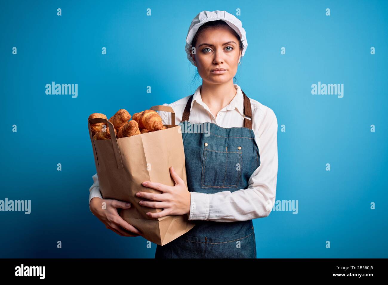 Young beautiful baker woman with blue eyes wearing apron holding paper ...