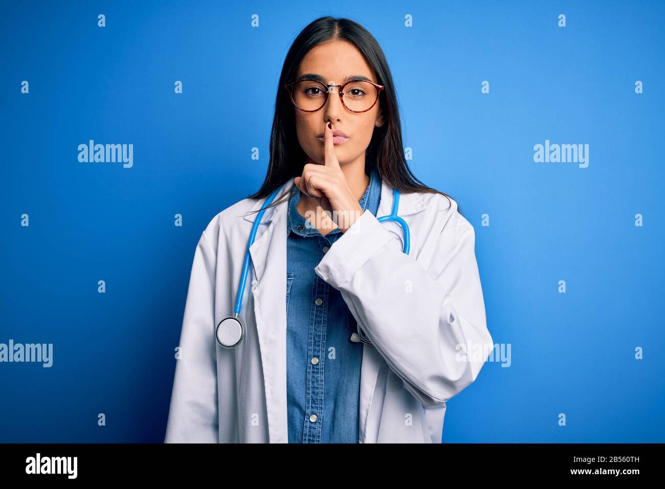 Young beautiful doctor woman wearing stethoscope and glasses over blue ...