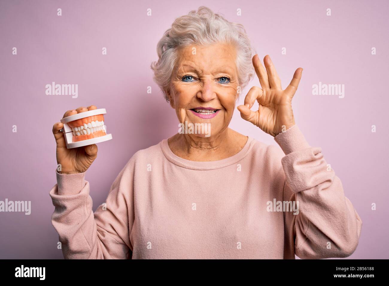 Senior beautiful grey-haired woman holding plastic denture teeth over ...