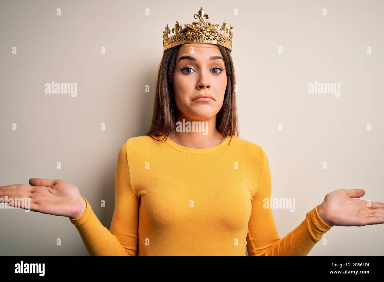 Young beautiful brunette woman wearing golden queen crown over white ...