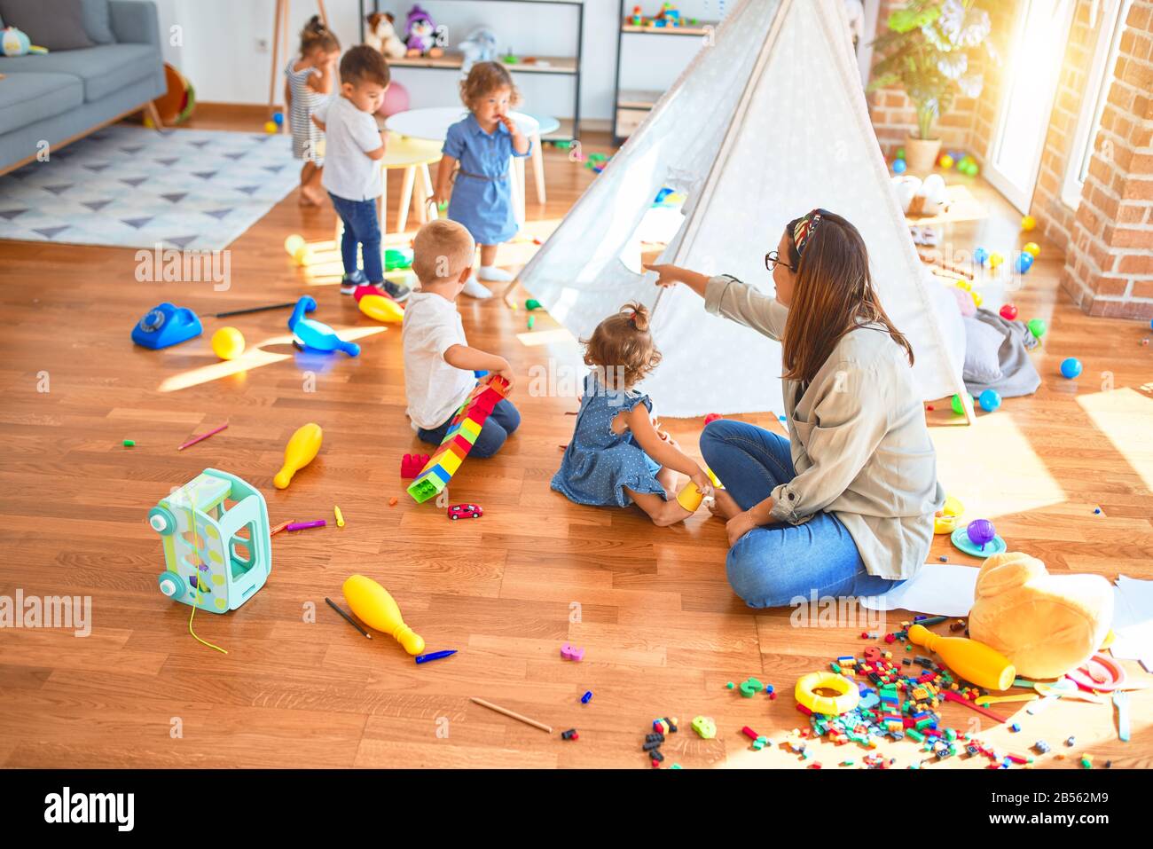 Beautiful teacher and group of toddlers playing around lots of toys at ...