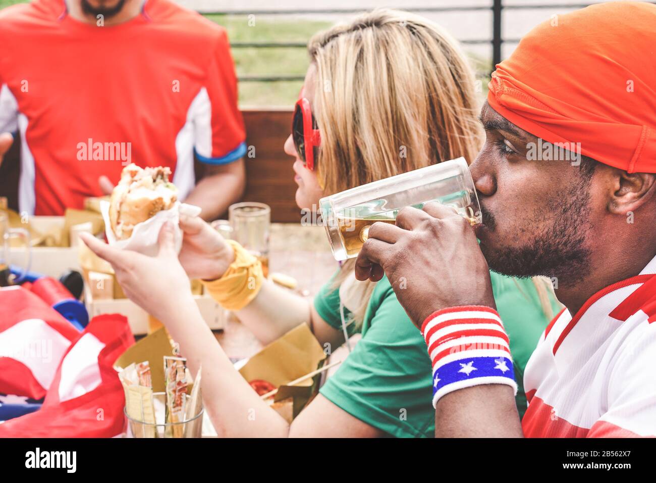 Multiracial american fans eating burgers and toasting beers in bar ...
