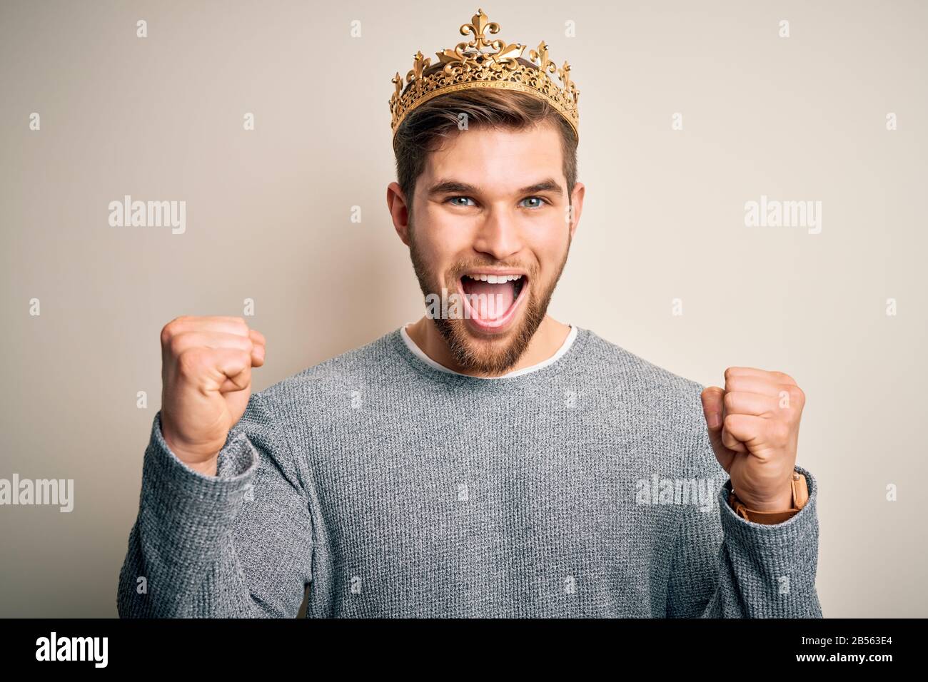 Young blond man with beard and blue eyes wearing golden crown of king ...