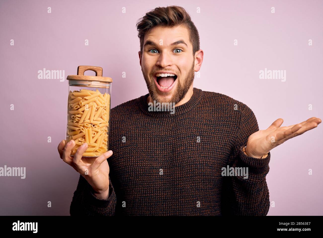 Young blond man with beard and blue eyes holding bottle of Italian dry ...