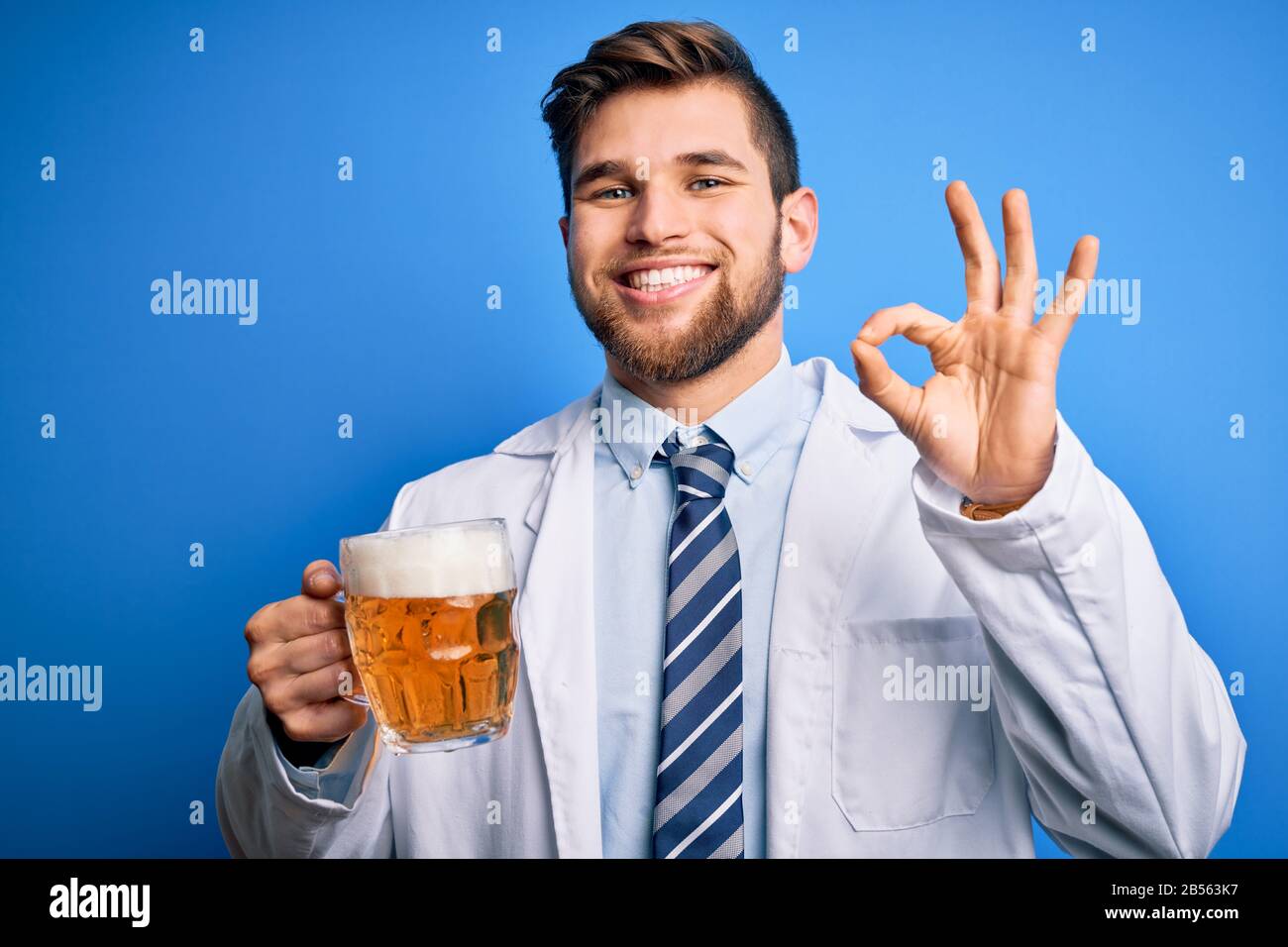 Young blond doctor man with beard and blue eyes wearing coat drinking ...